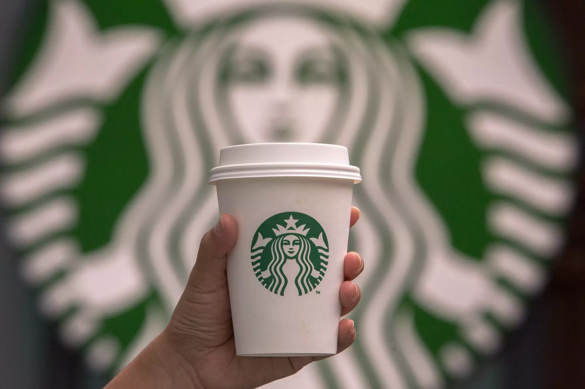 Kezében egy csésze kávét a Starbucks logó előtt.