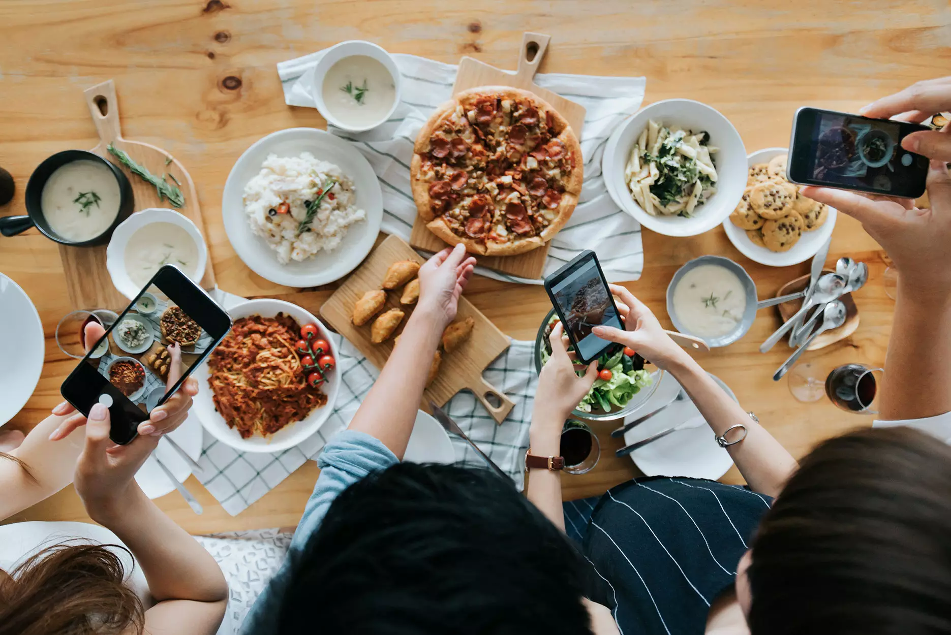 पार्टी के दौरान स्मार्टफोन के साथ मेज पर भोजन की तस्वीरें लेते दोस्तों का समूह