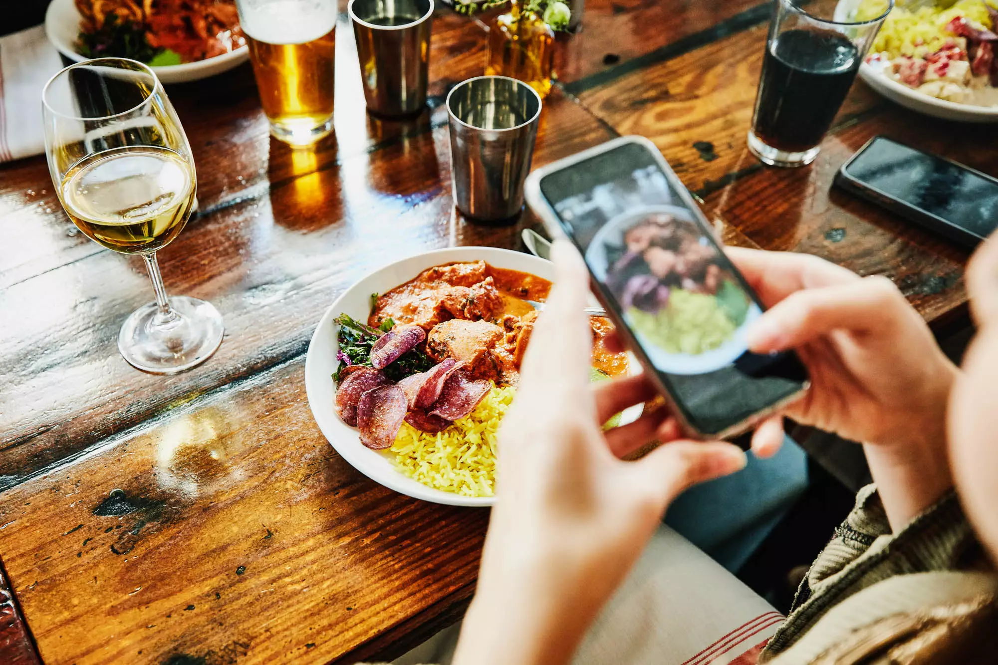 रेस्टॉरंटमध्ये मित्रांसोबत जेवण करताना स्मार्टफोनसह जेवणाचा फोटो घेत असलेली महिला