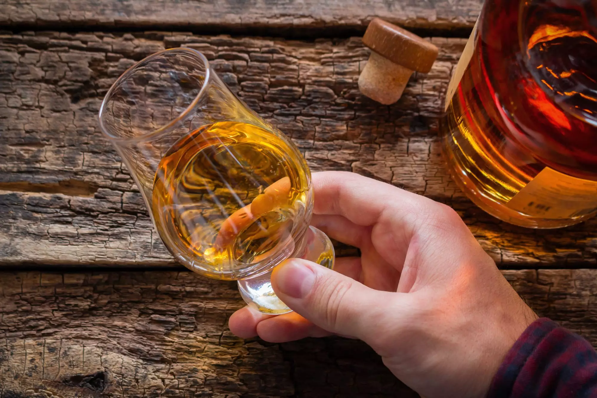 ruka drží whisky ve sklenici k ochutnání na dřevěném pozadí