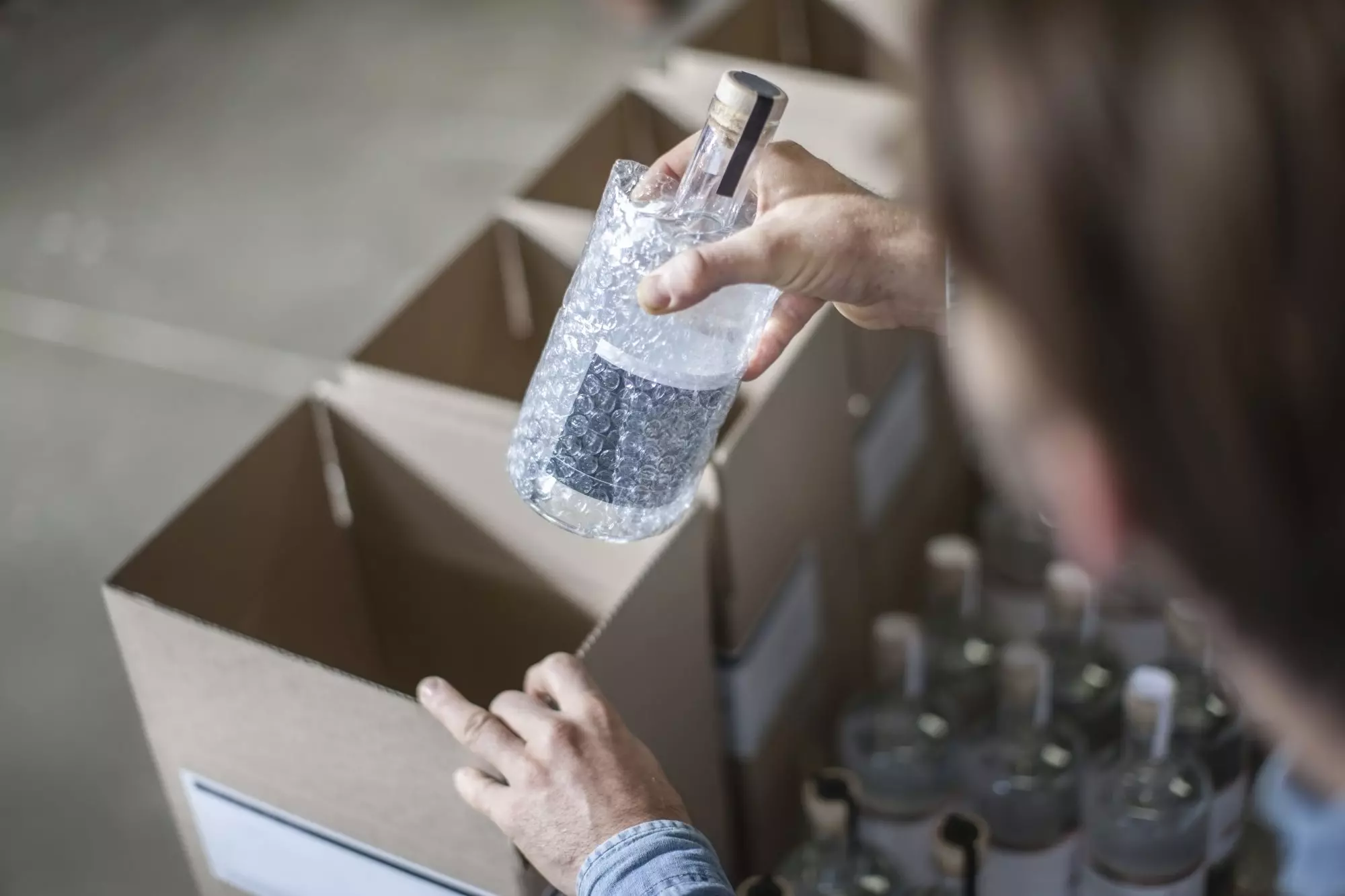 Homem colocando garrafa de licor em caixa de papelão